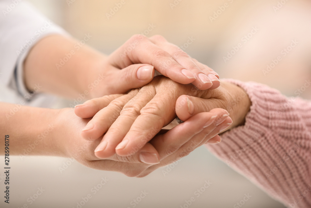 Nurse holding hands of elderly woman against blurred background ...