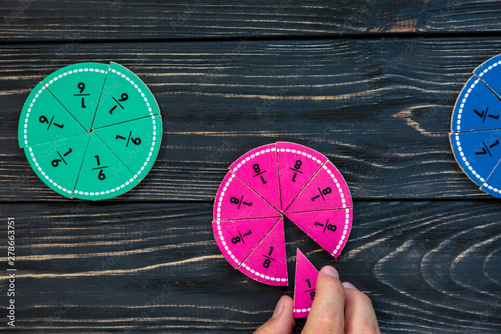 Kids hand moves colorful math fractions on dark wooden background or ...