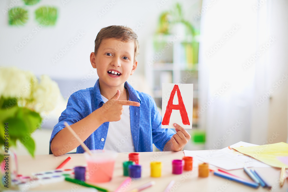 happy child at the table with school supplies smiles funny and learns ...
