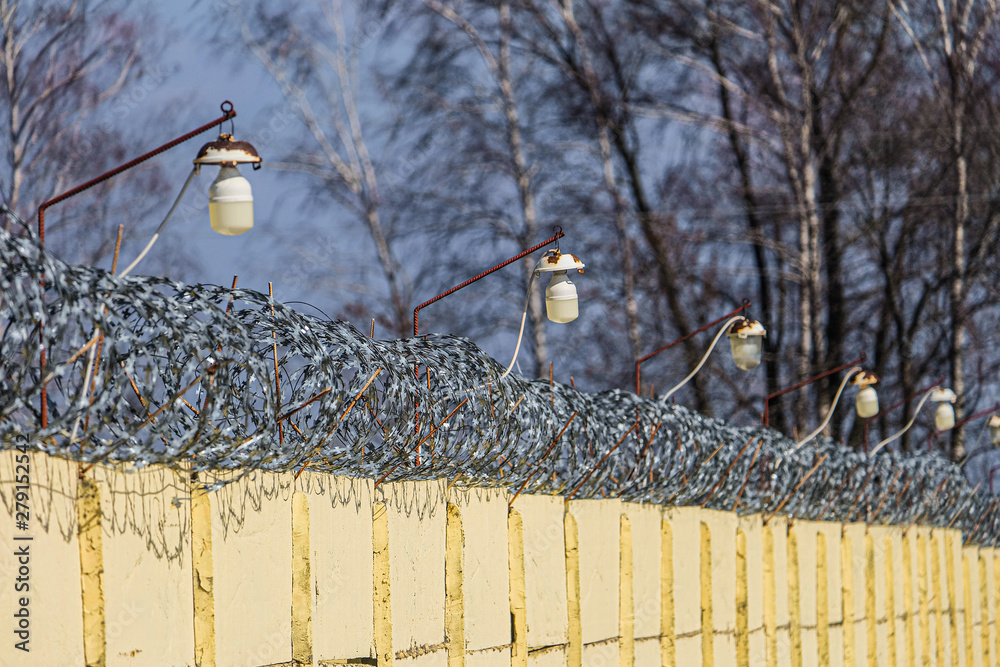 Barbed wire on a concrete fence with light lamps. Day view with limited ...