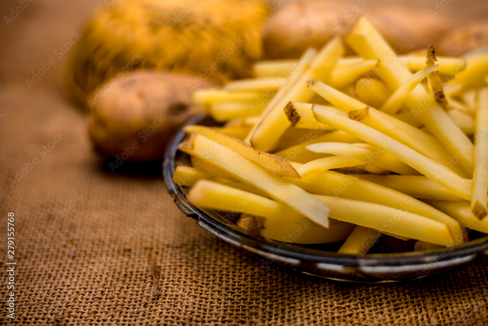Raw cut french fries in a transparent glass plate along with raw potato ...