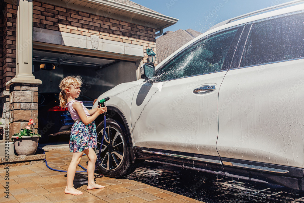 Foto de Cute preschool little Caucasian girl washing car on driveway in ...