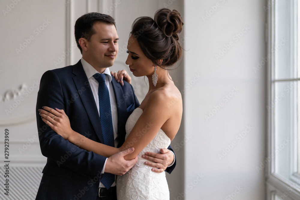 embraces newlyweds in classic white interior. Bride and groom next to ...