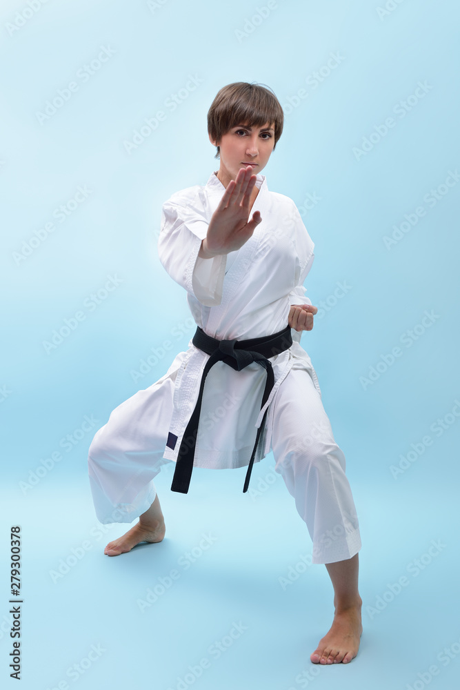 Young karate woman in a white kimono with black belt demonstrates ...