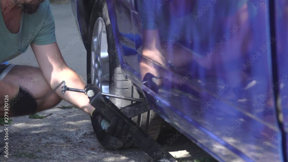 the man picks up the car Jack and Unscrew the rear wheel. technical ...