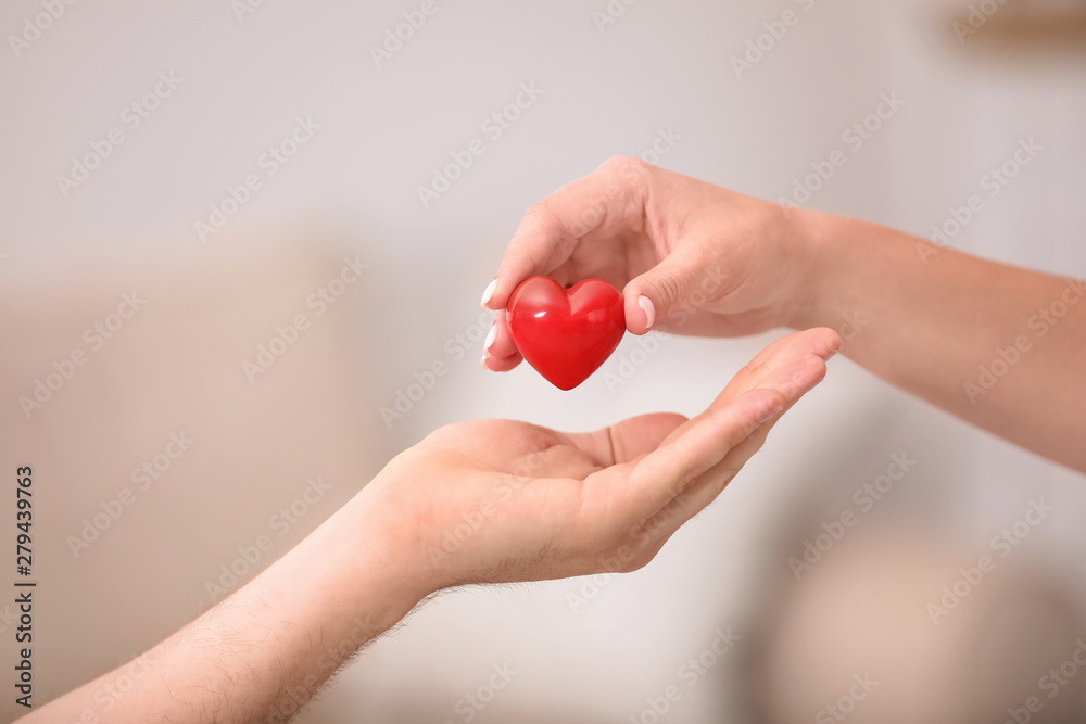 Woman giving red heart to man on blurred background, closeup. Donation ...