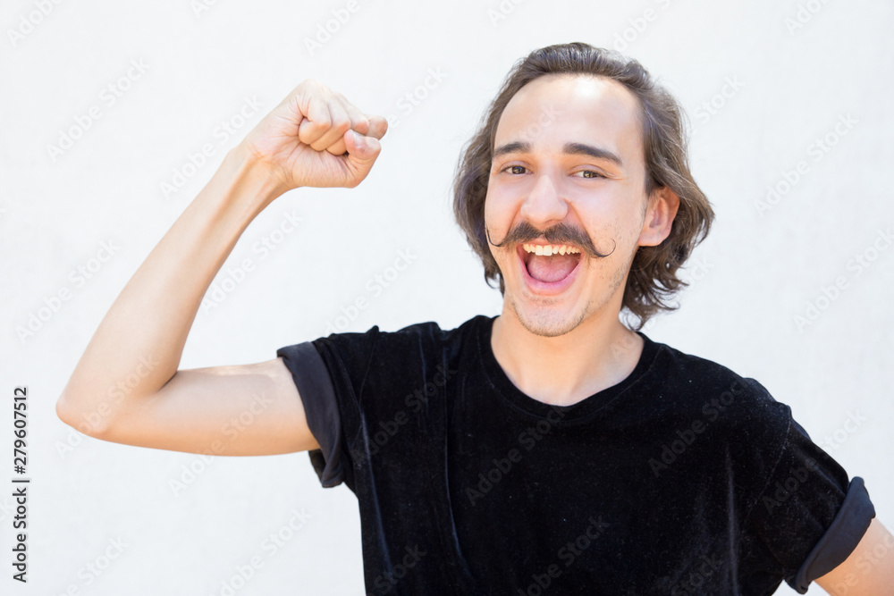 Smiling thin young man with mustache showing biceps. Sportsman beginner ...