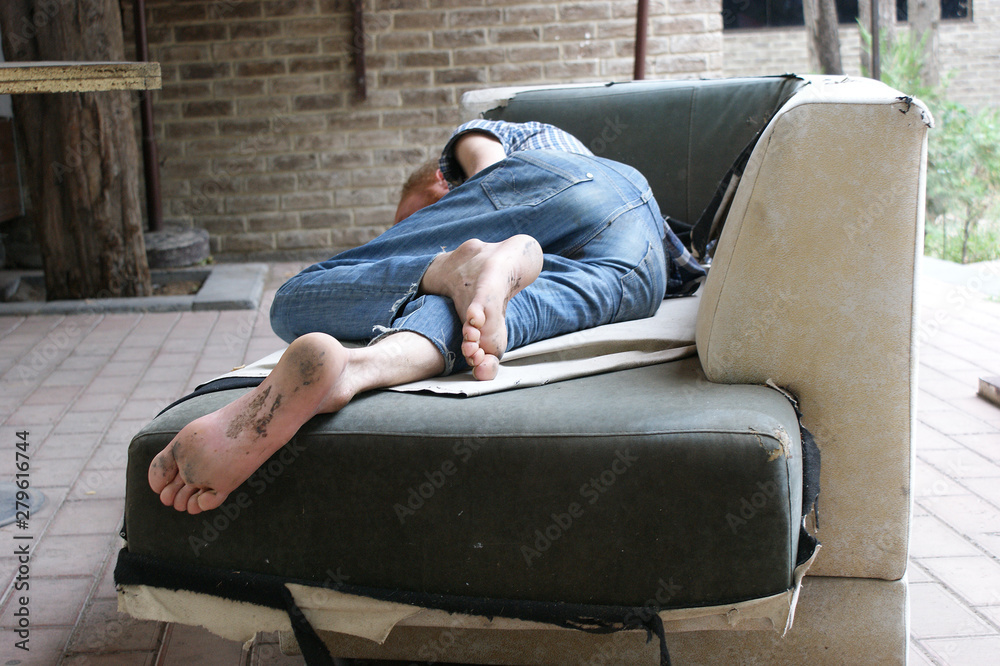 poor man lying on an old couch. poor man with dirty feet and no shoes ...