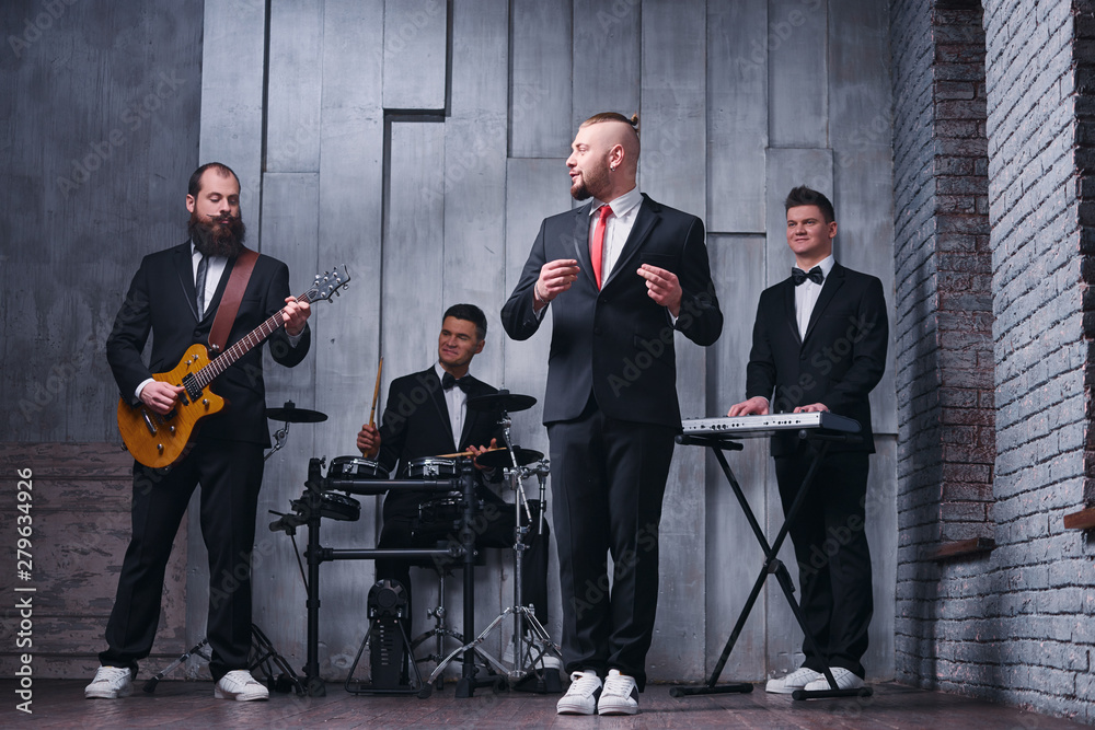 Music band and fashion. Handsome young men in suits playing rock and ...