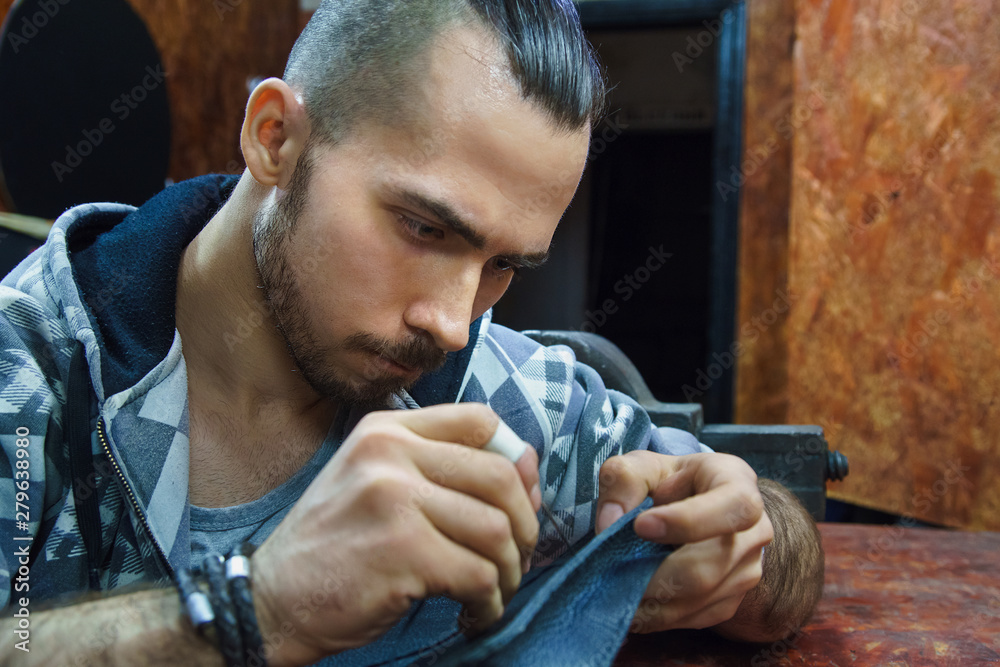 Craftsman intently works with leather. Tanner sews leather goods ...