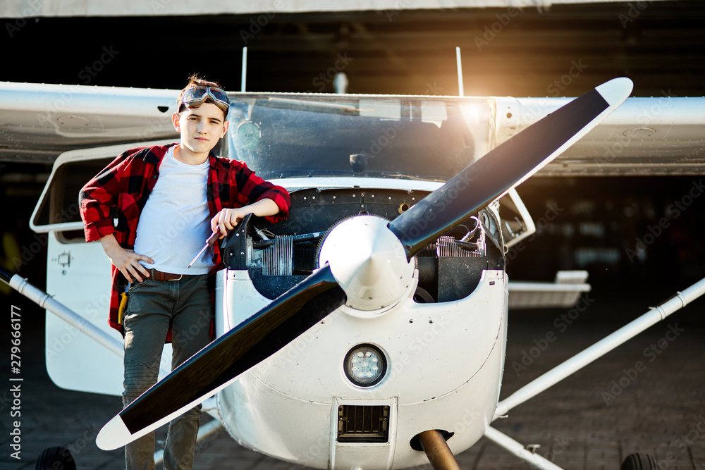 boy leans on plane, stands with serious face expression, feels tired ...
