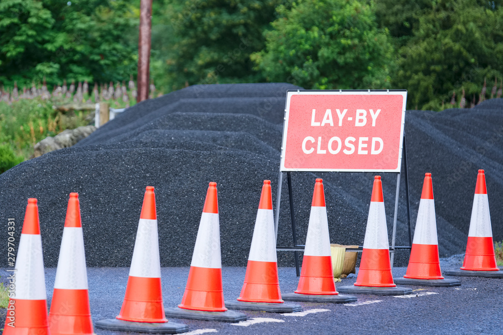 Road lay by closed sign with pile of black tar and red traffic cones ...