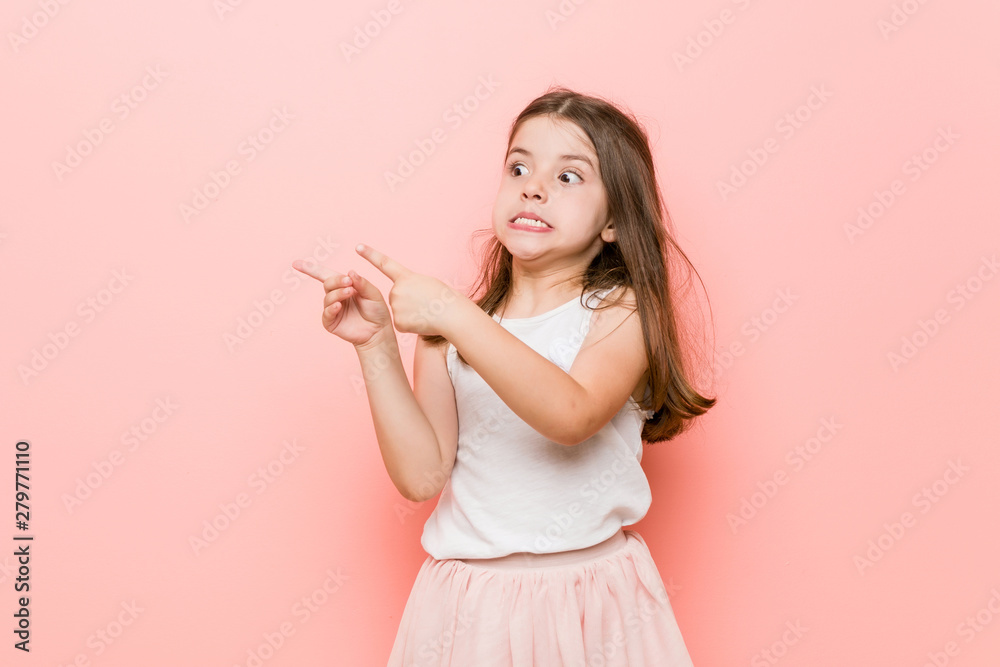 Little girl wearing a princess look shocked pointing with index fingers ...