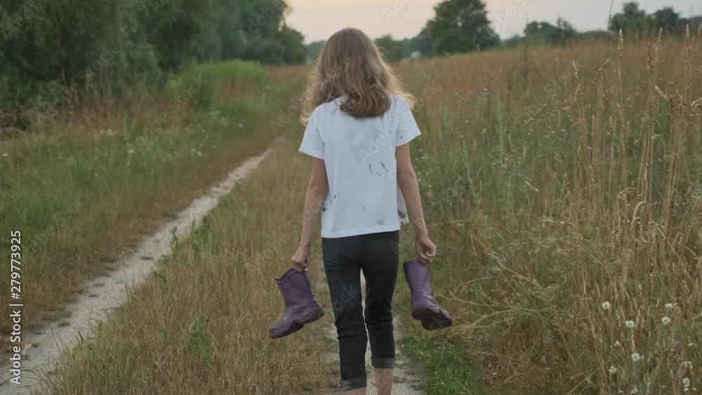 Little girl walking on a rural road with boots in her hands. Happy ...
