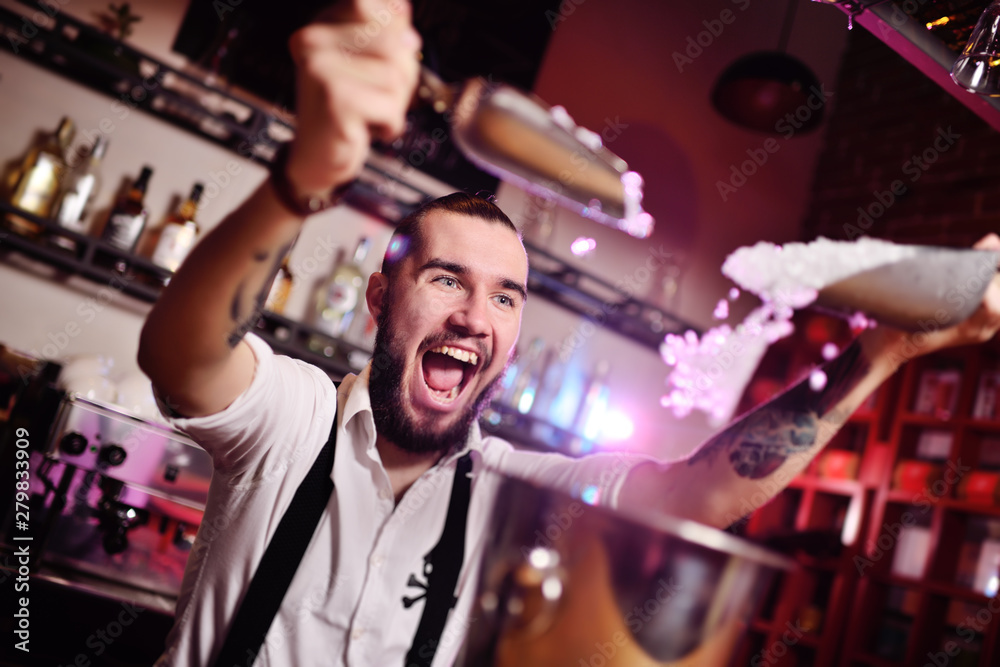 a handsome bearded bartender in a white shirt pours ice for cocktails ...