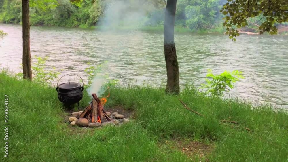 Bonfire and cast-iron cauldron on the background of a forest river in ...