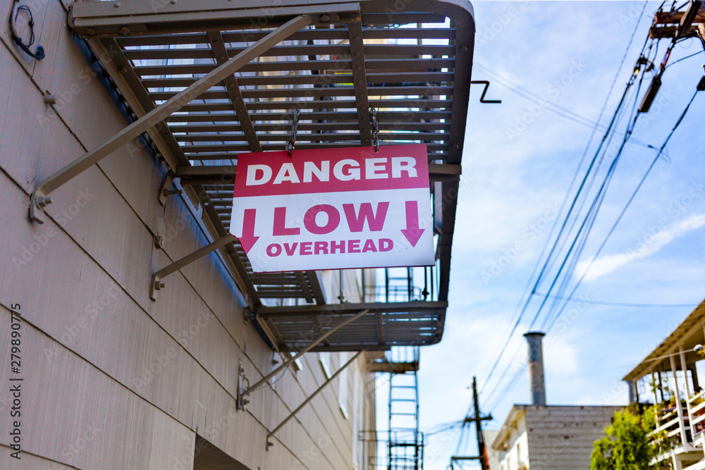 OSHA compliant DANGER LOW OVERHEAD sign hanging from urban building ...
