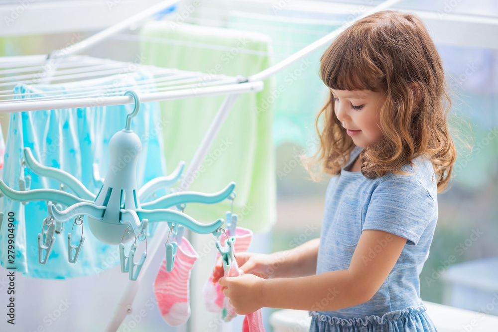 Child in laundry room. Clean washed clothes on drying rack. Mother's ...