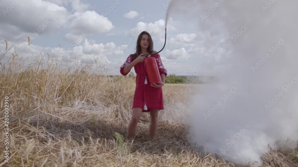 Attractive woman with long hair using fire extinguisher on the wheat ...