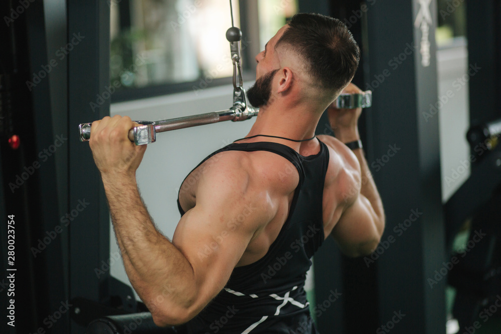 A young athlete trains in the gym. Shows the muscles of the back and ...