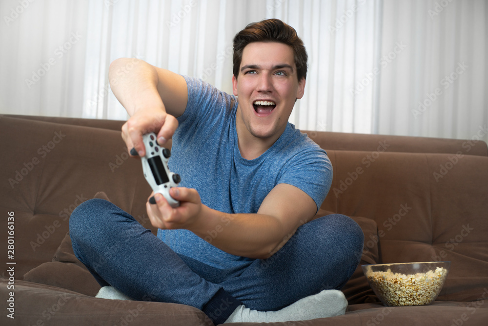 young handsome man playing video game sitting on comfy sofa holding ...