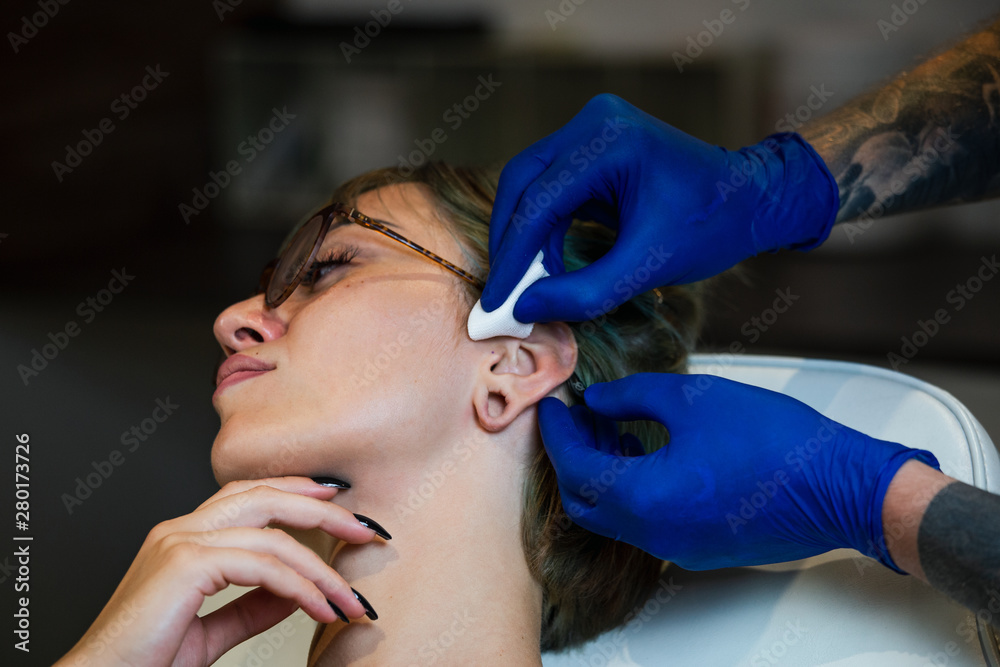 Portrait of a woman getting her ear pierced. Man showing a process of ...