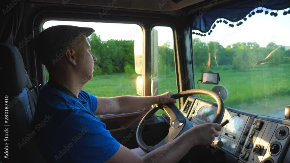 Profile of lorry driver riding through countryside in evening. Man in ...