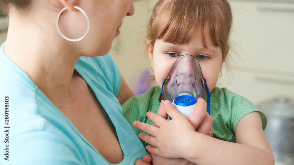 woman makes inhalation to a child at home. brings the nebulizer mask to ...