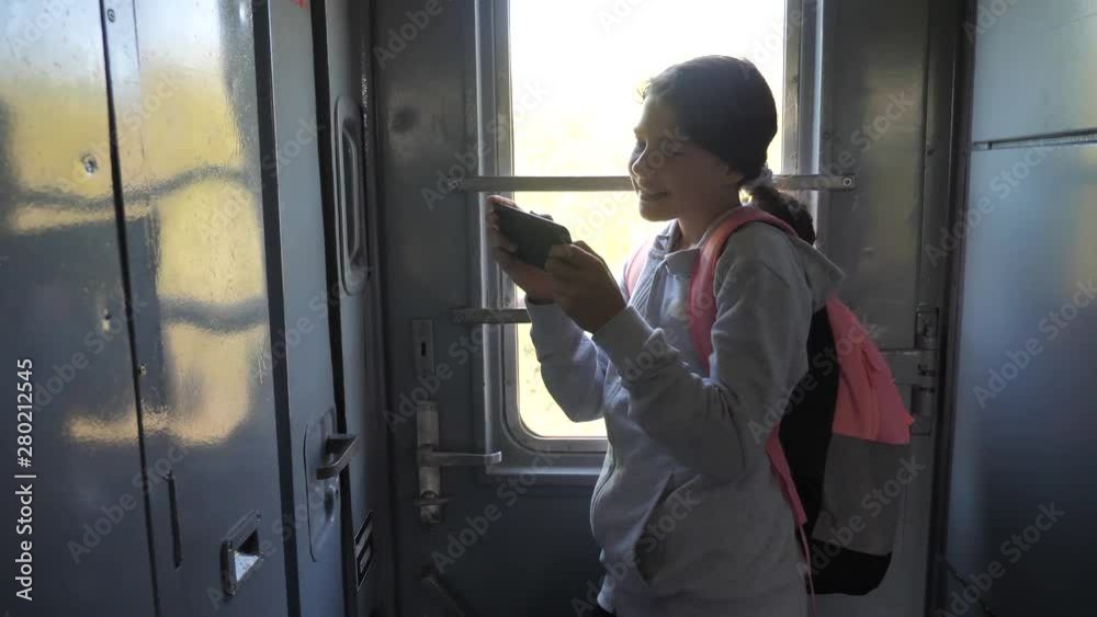 teenager girl traveler with backpack stands by the window of the train ...