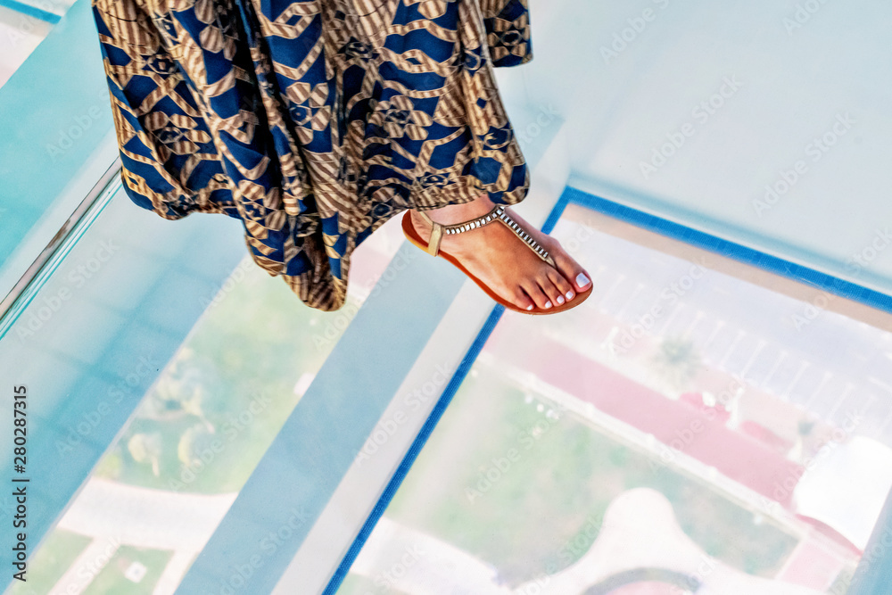 Woman stepping fith her feet on the glass floor at the Frame high above ...