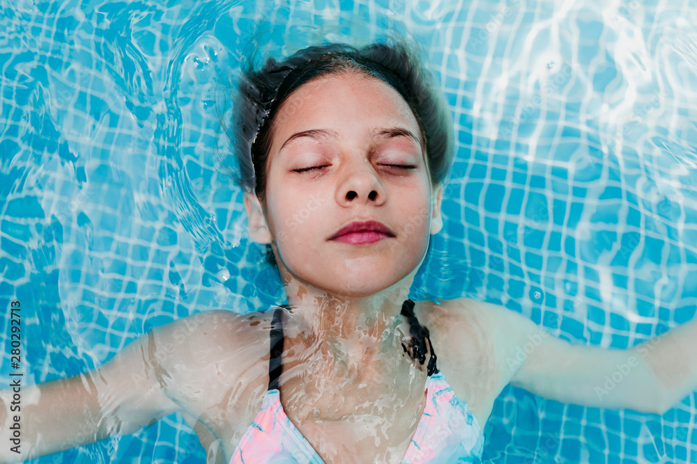 beautiful teenager girl floating in a pool and looking at the camera ...