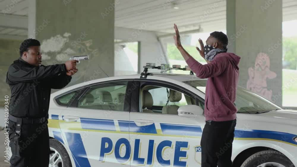 Serious policeman with pistol standing near the car with a robber in ...
