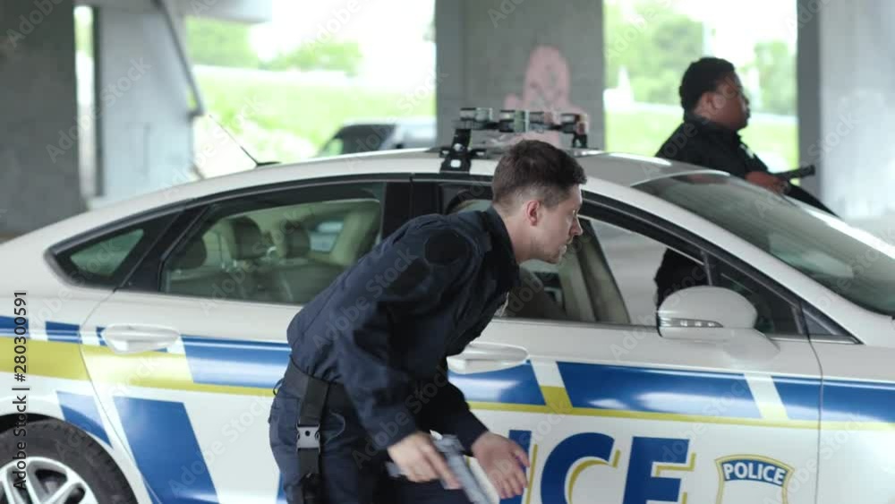 Serious young policemen with pistol standing near the car arrest robber ...