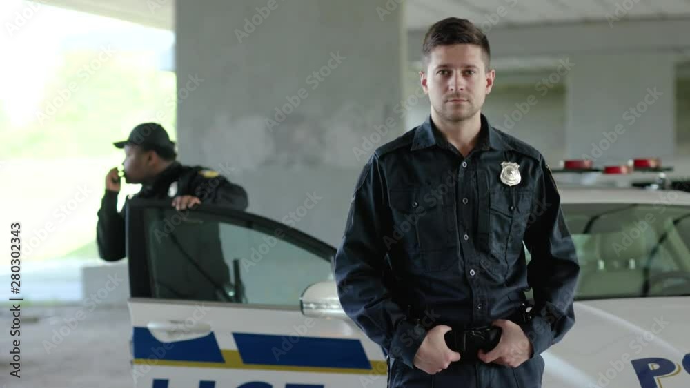 Portrait two young man cops stand near patrol car look at camera ...