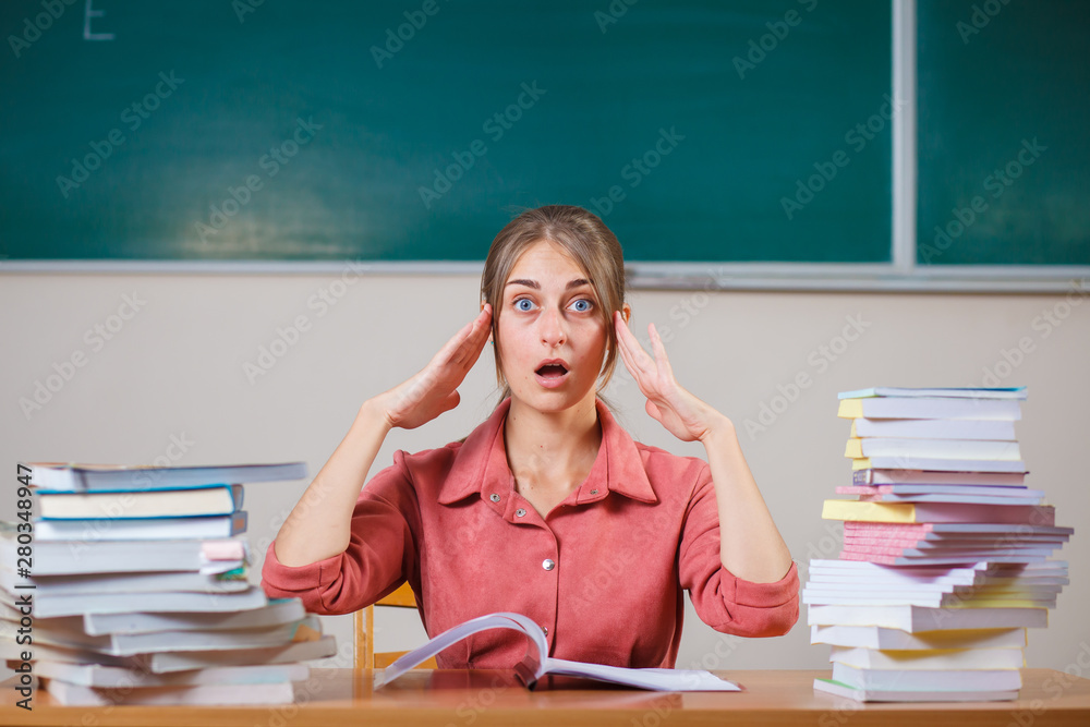 Teacher surrounded by books sitting in school classroom.Emotional ...