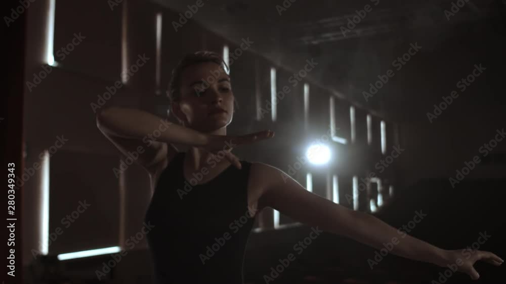 Graceful woman ballerina in a dark dress on a dark stage of the theater ...