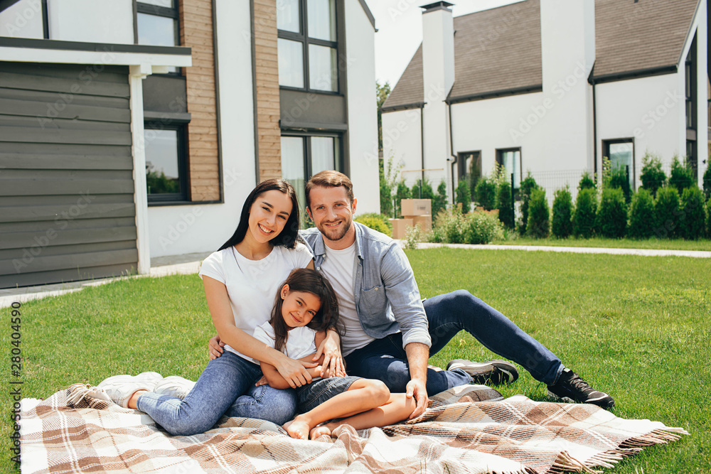 Family sitting on lawn in backyard, big modern house on background ...