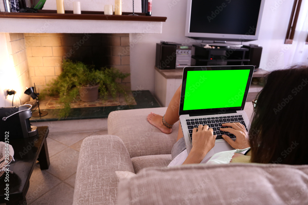 A young woman works on her laptop with the green screen at home sitting ...