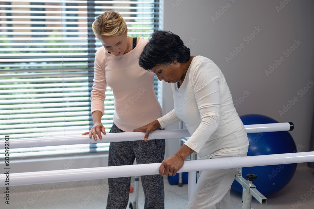 Female physiotherapist helping patient walk with parallel bars in the ...
