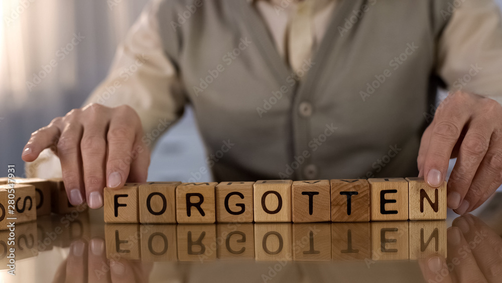 Elderly male making word forgotten of wooden cubes on table, dementia ...