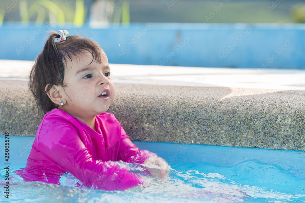 Baby girl of two years old plays in a swimming pool. She is happy and ...