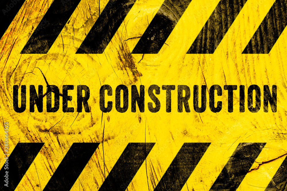 Under construction warning sign text with yellow black stripes painted ...