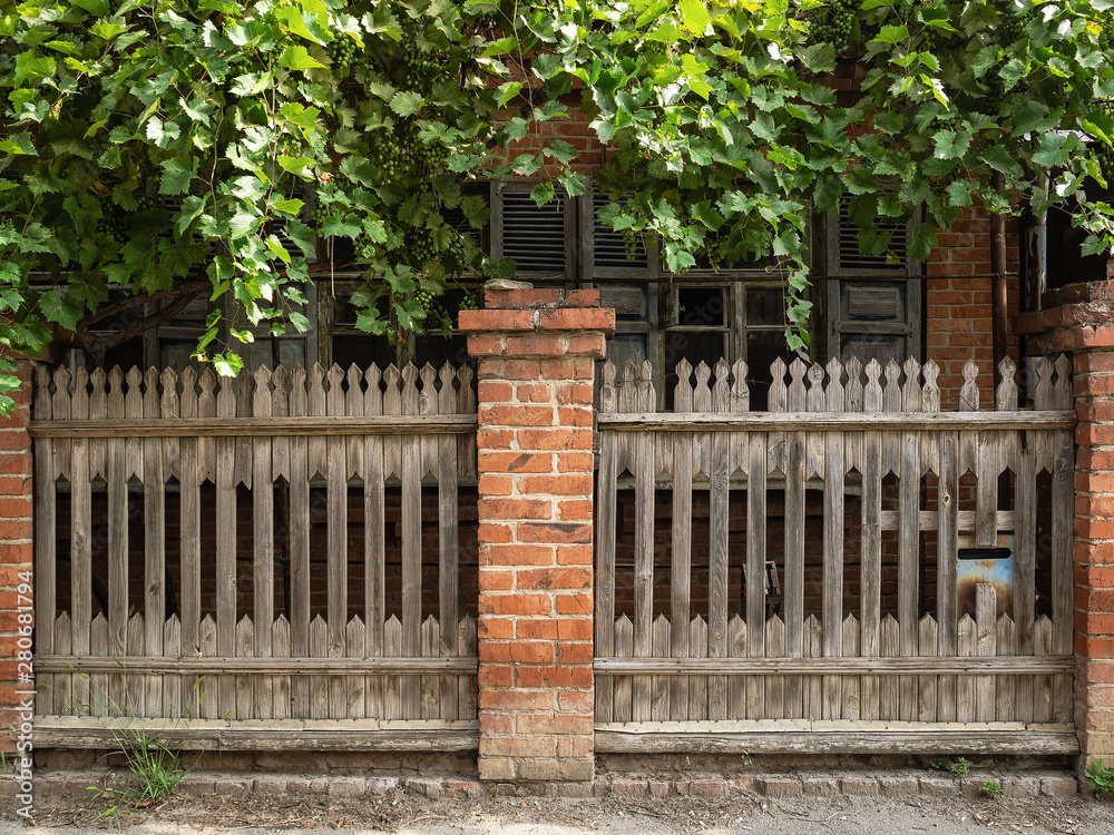 Outdated house with wooden and brick fence. From above grow thick ...