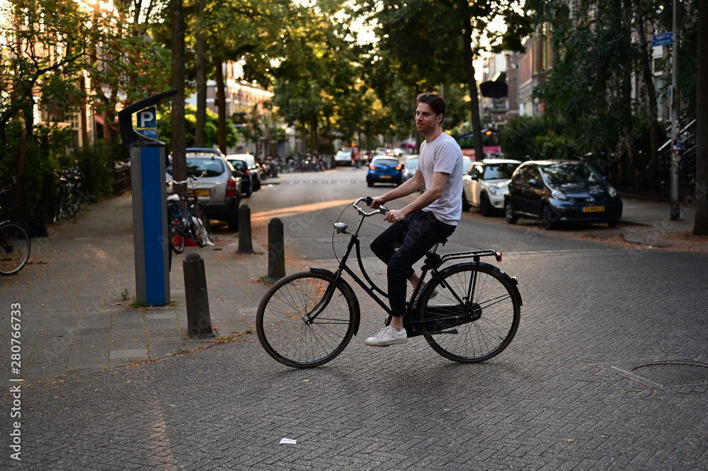 Happy young man riding a bicycle through some traditional Dutch streets ...