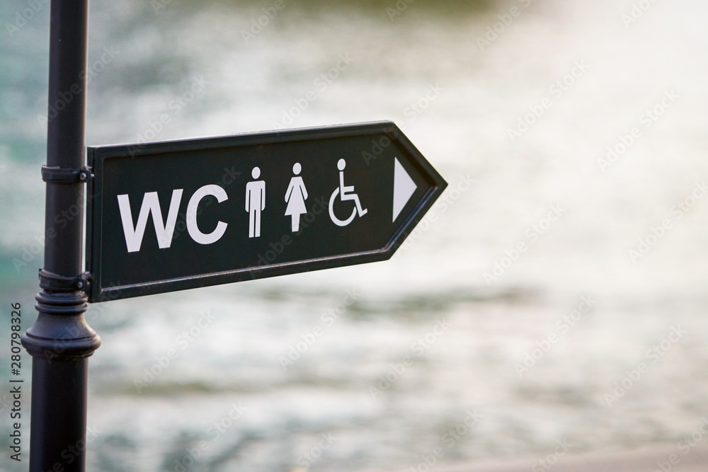 WC logo, sign of public toilets in the street against water background ...