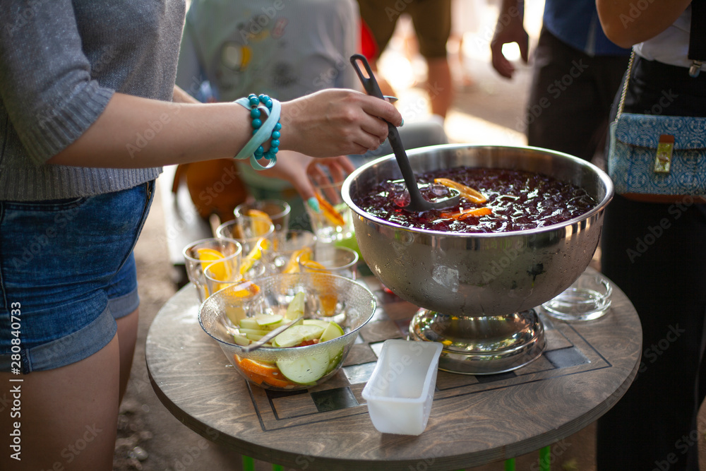 The girl pours a punch into a glass. Party in the open air. Light ...