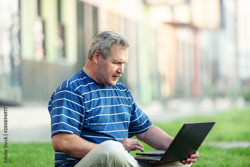 Beautiful adult man sitting on the lawn in the city with laptop. Of ...