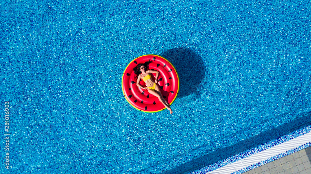 Young woman relaxing on watermelon in hotel resort pool. Top view of ...