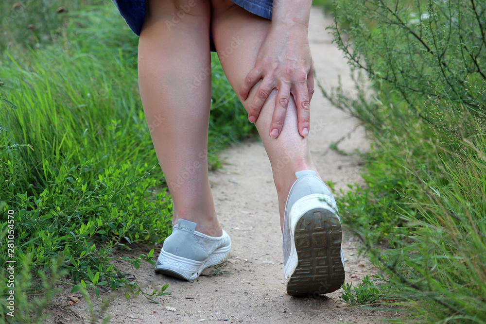 Ankle sprain, woman grabbed her leg while walking on a summer nature ...