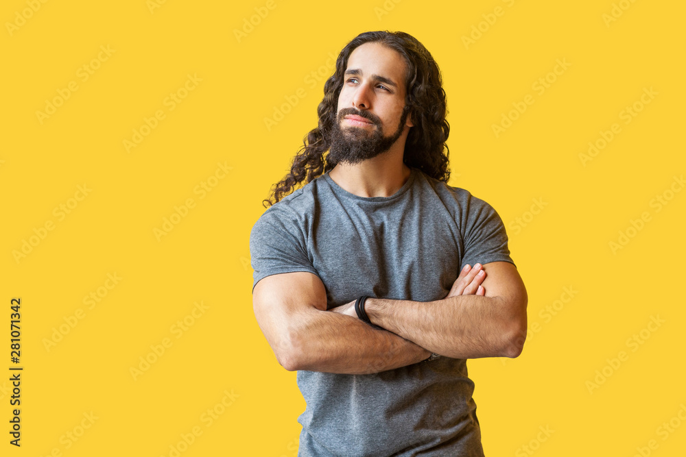 Portrait of thoughtful bearded young man with long curly hair in grey ...
